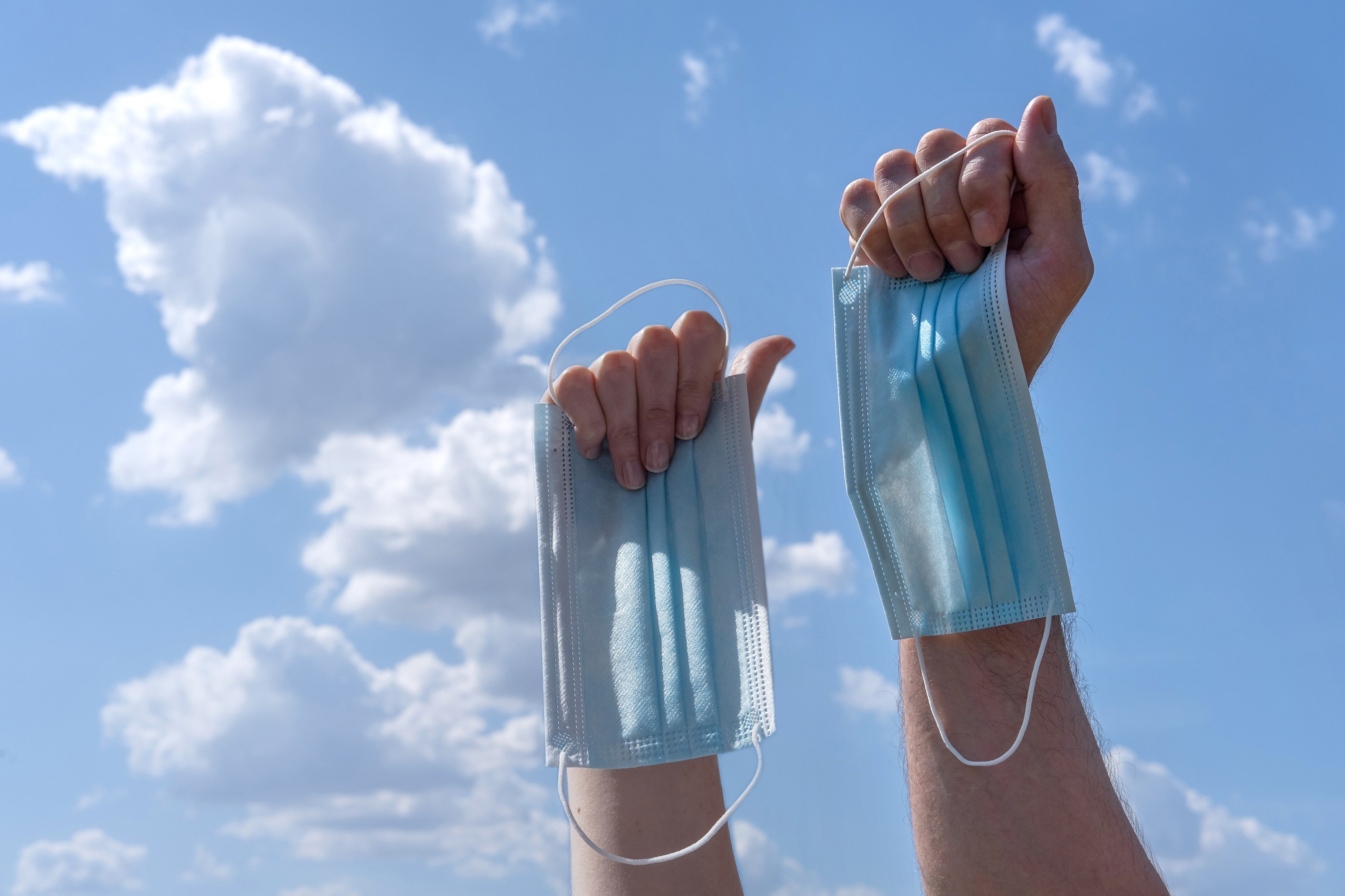 Two hands holding face mask on blue sky background (588429 ...