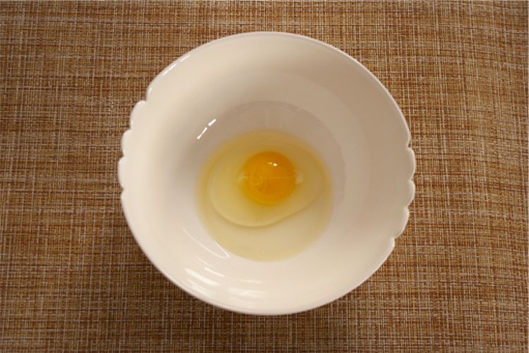 Egg without shell in a white bowl on the table light brown