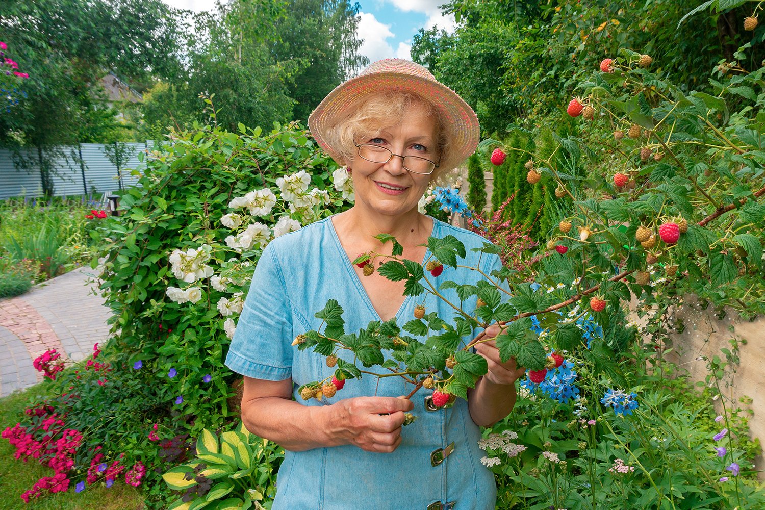 Woman gardener in glasses and a hat stands in the garden.
