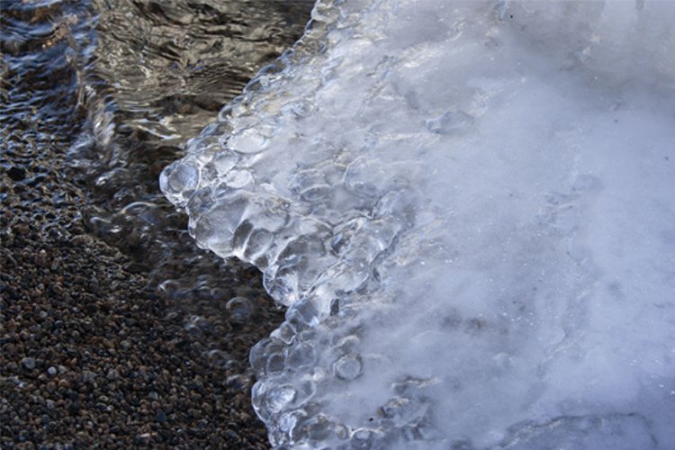 Abstract background. Ice, water, pebbles on the shore.Nature