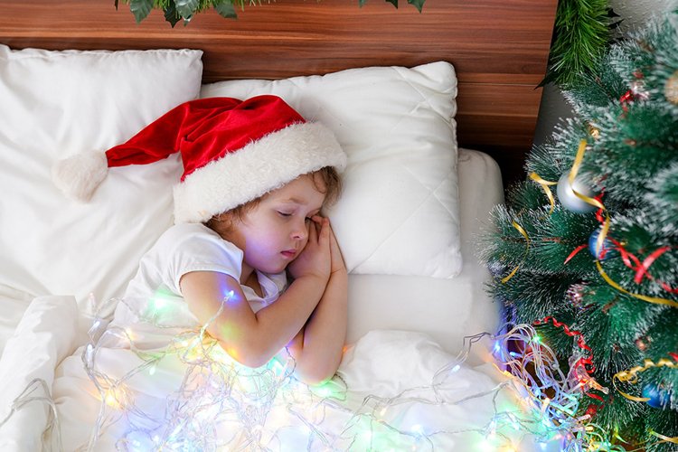 child girl sleeping in comfortable bed near Christmas tree