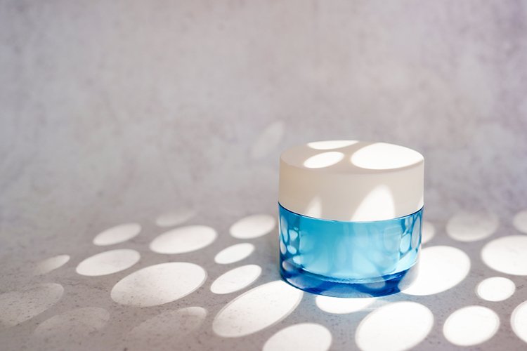 Blue glass moisturizer cream, shadows play on light concrete