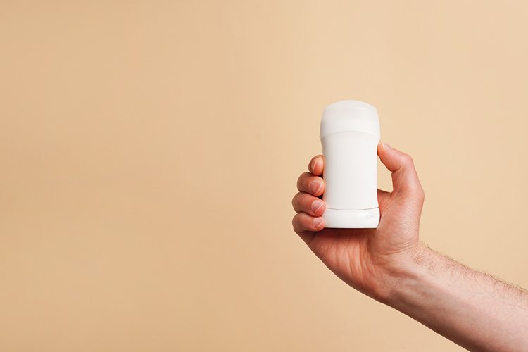 Male hand holding white deodorant on beige background