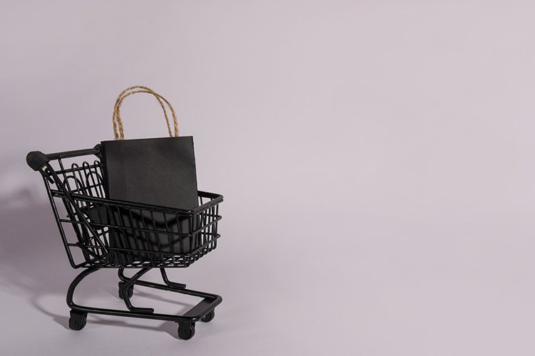 Black shopping cart with paper bag on gray background