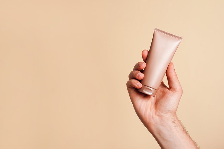 Male hand holding unbranded beige tube with lotion