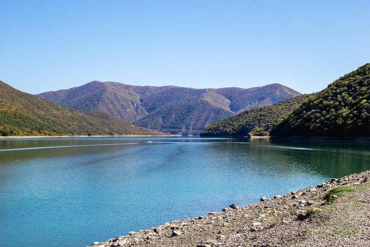 Scenic view on bank of lake with blue water and mountains.